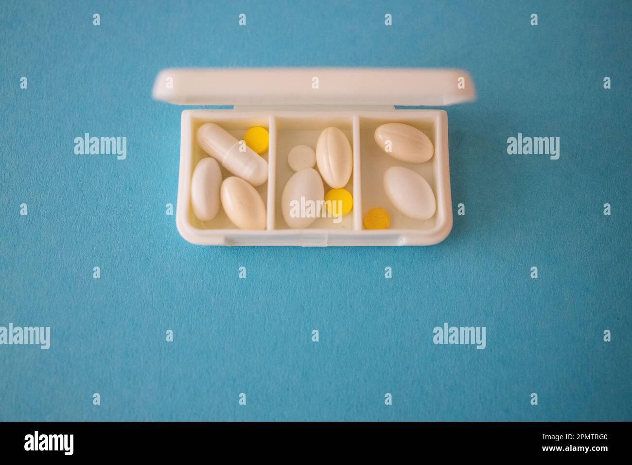 different capsules lie in a white open pill box on a blue background ...