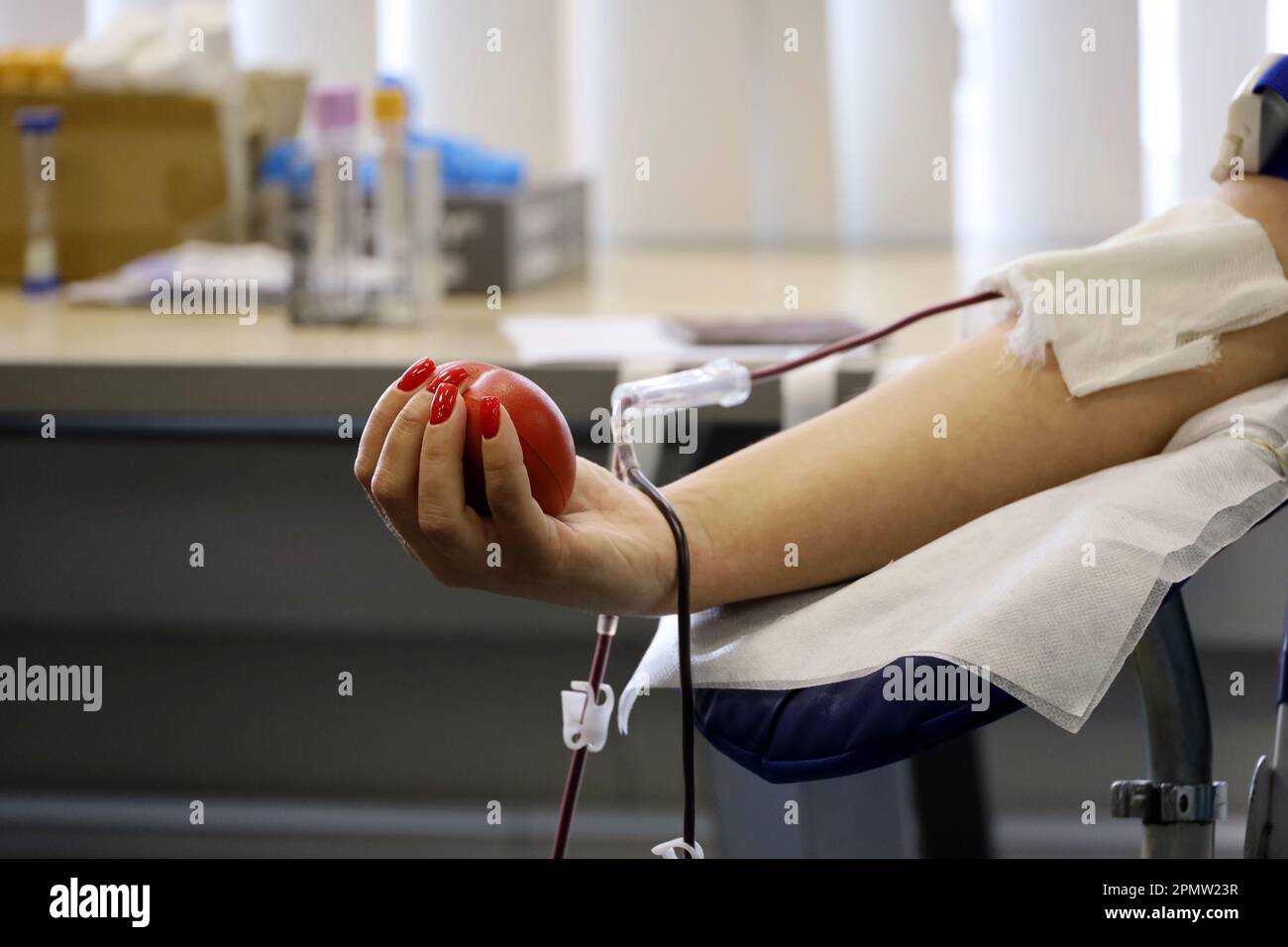 Woman blood donor in chair during donation with red bouncy ball in hand ...