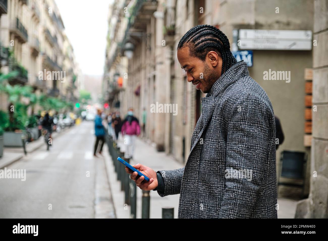 Man smiling while using his mobile phone standing outside on the street ...
