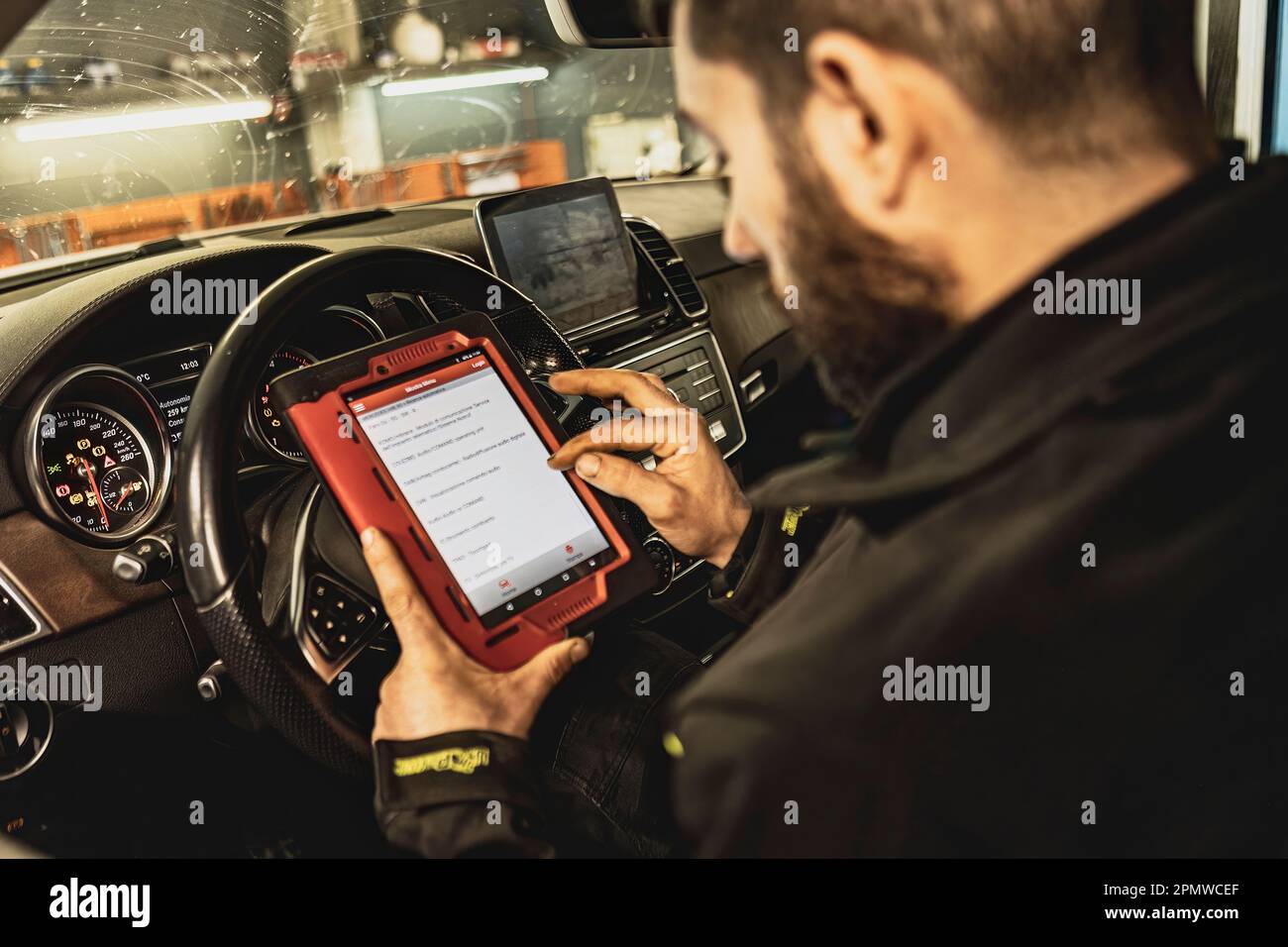 A mechanic's hands use a diagnostic tool to troubleshoot a modern car's ...