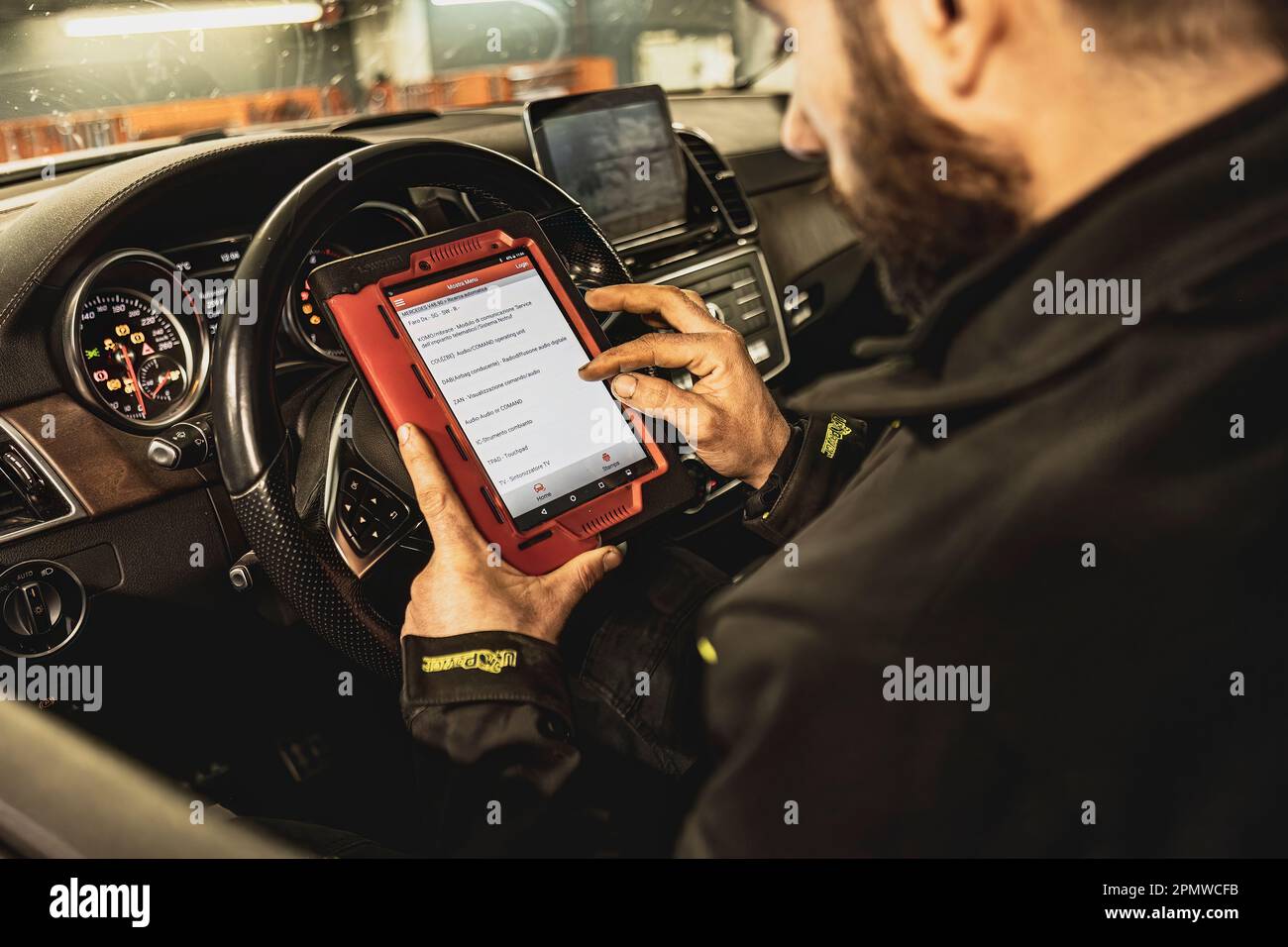 A mechanic's hands use a diagnostic tool to troubleshoot a modern car's ...