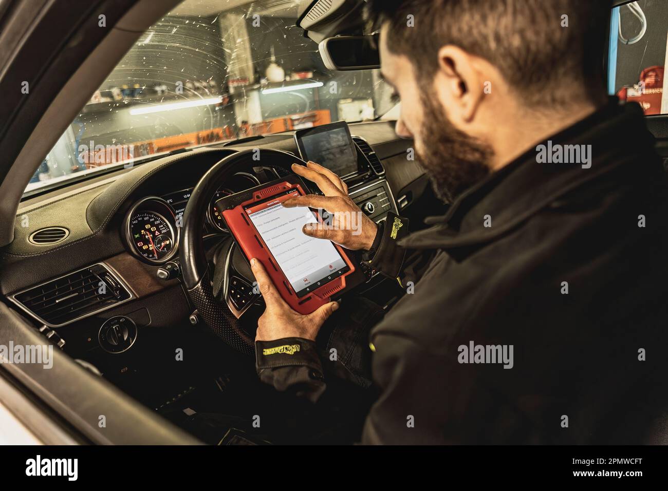 A mechanic's hands use a diagnostic tool to troubleshoot a modern car's ...
