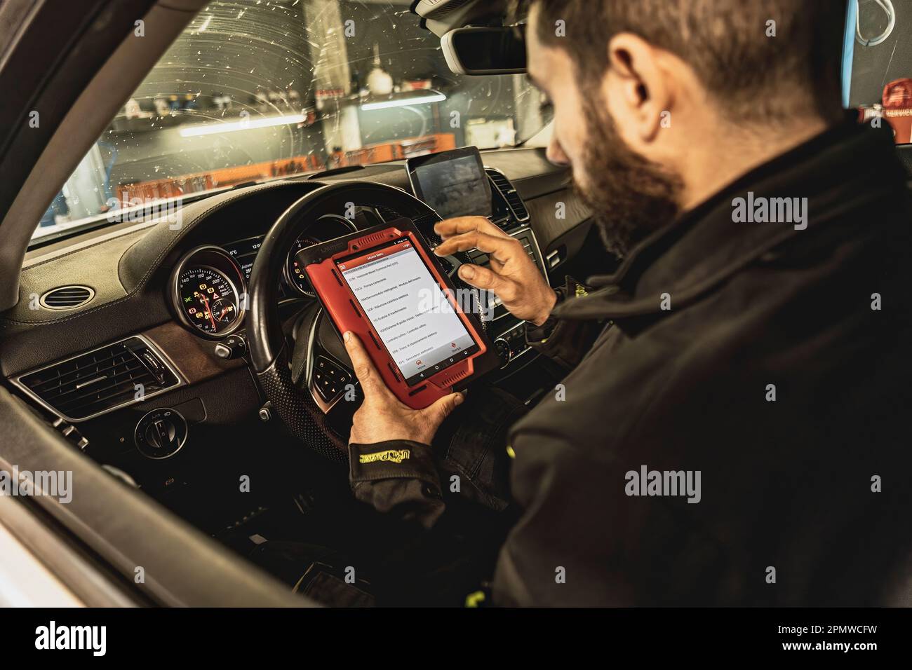 A mechanic's hands use a diagnostic tool to troubleshoot a modern car's ...