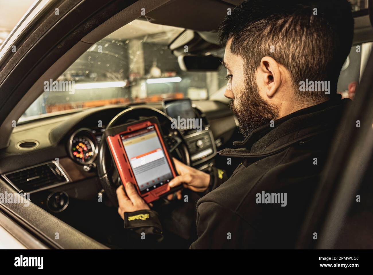 A mechanic's hands use a diagnostic tool to troubleshoot a modern car's ...