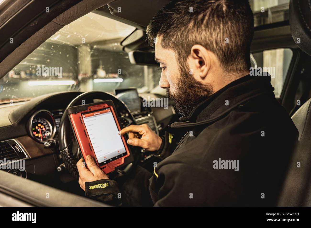 A mechanic's hands use a diagnostic tool to troubleshoot a modern car's ...