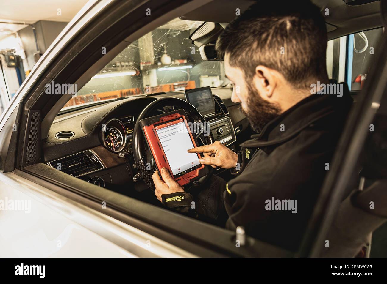A mechanic's hands use a diagnostic tool to troubleshoot a modern car's ...