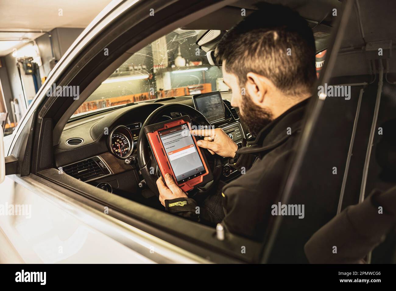 A mechanic's hands use a diagnostic tool to troubleshoot a modern car's ...