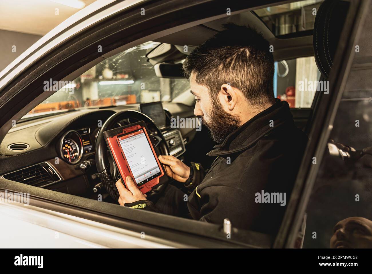 A mechanic's hands use a diagnostic tool to troubleshoot a modern car's ...