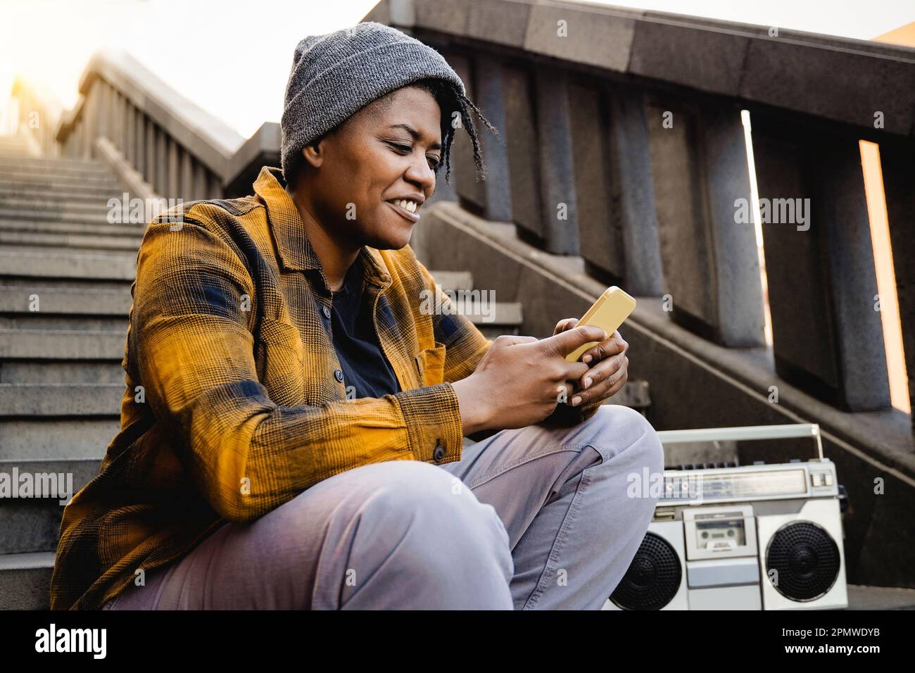 Happy African girl with hip-hop style using mobile phone next to ...