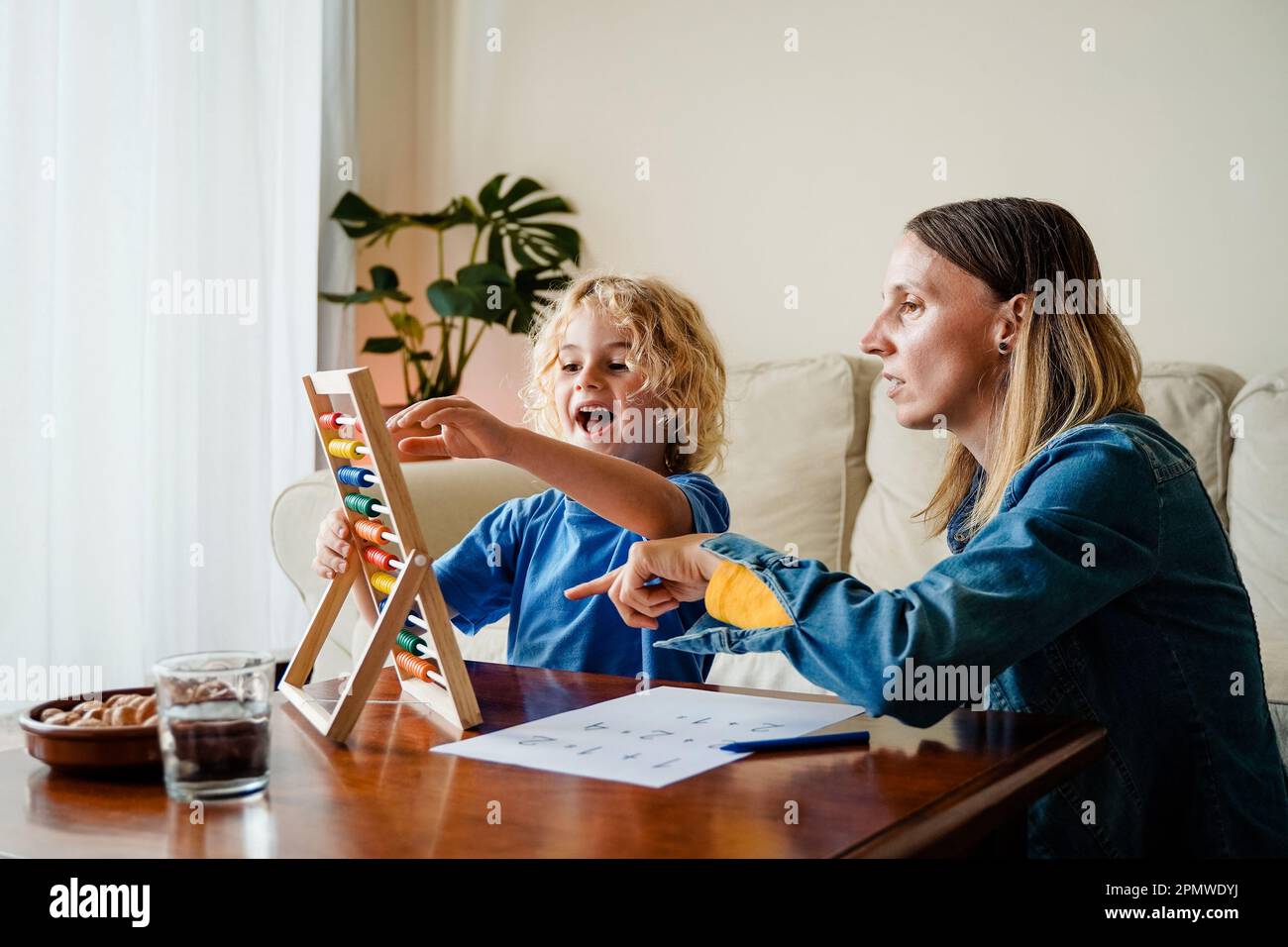 Mother and son studying math with abacus for school class inside home ...