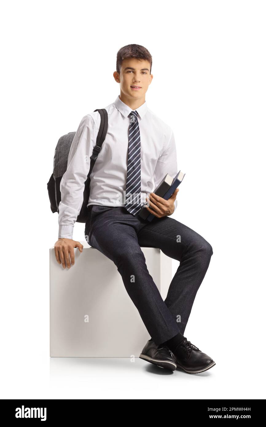 Male student in a school uniform holding books and sitting on a white ...