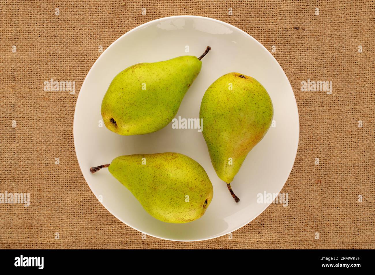 Three organic pears with ceramic plate on jute cloth, macro, top view ...