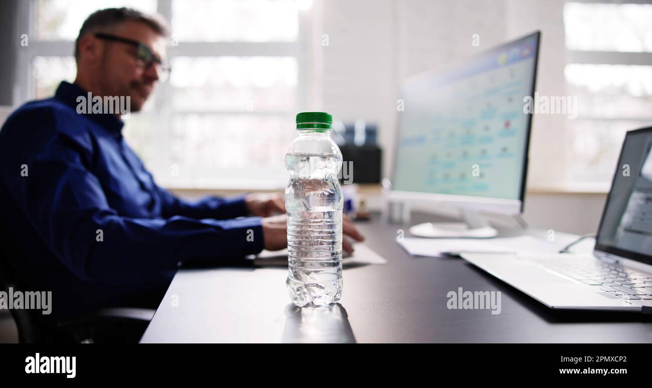 Water Bottle On Desk And Man In Background Using Computer Stock Photo ...