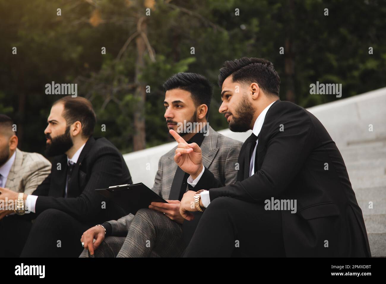Business people outdoor meeting. Several men in suits sit on the steps ...