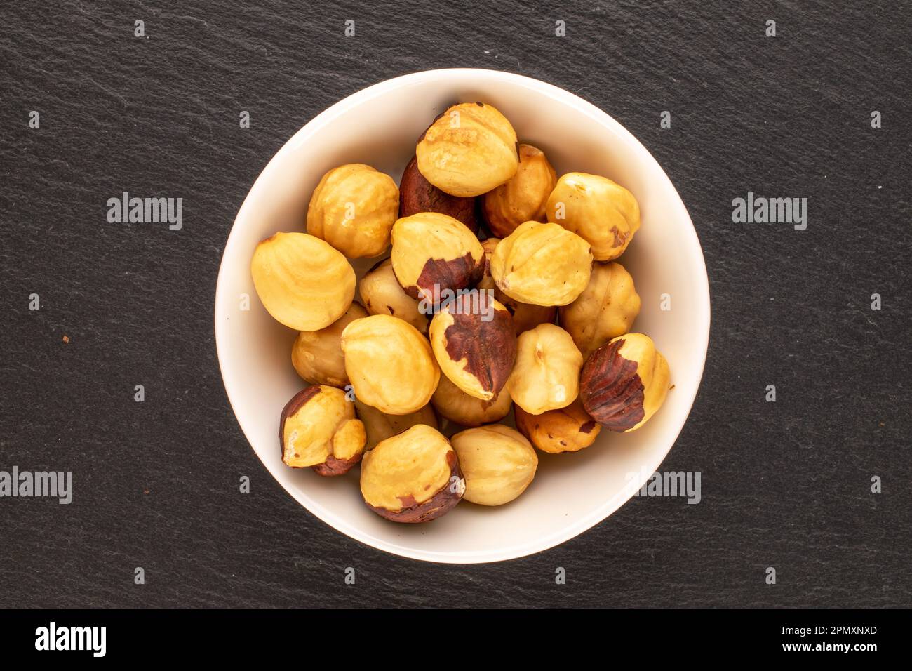 Roasted hazelnuts with white ceramic saucer on slate stone, macro, top ...