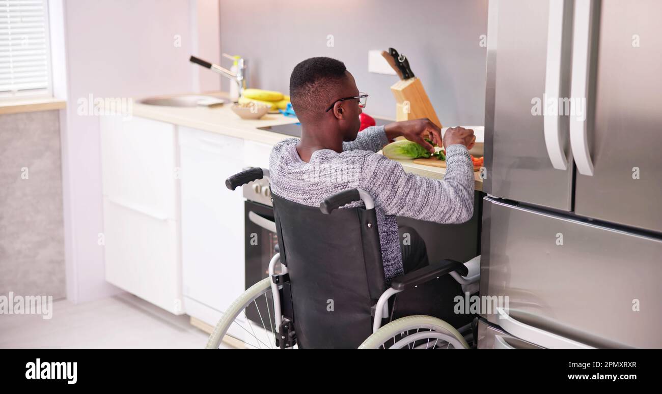 Young Disabled Man Sitting On Wheel Chair Preparing Food In Kitchen ...