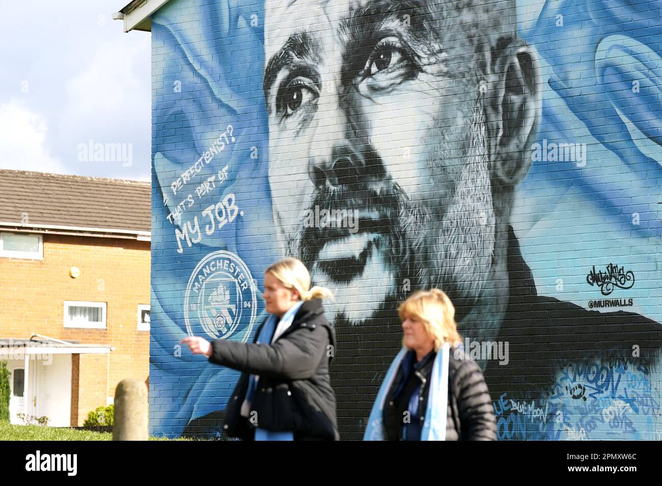 Manchester City fans walk past a mural of Manchester City manager Pep ...