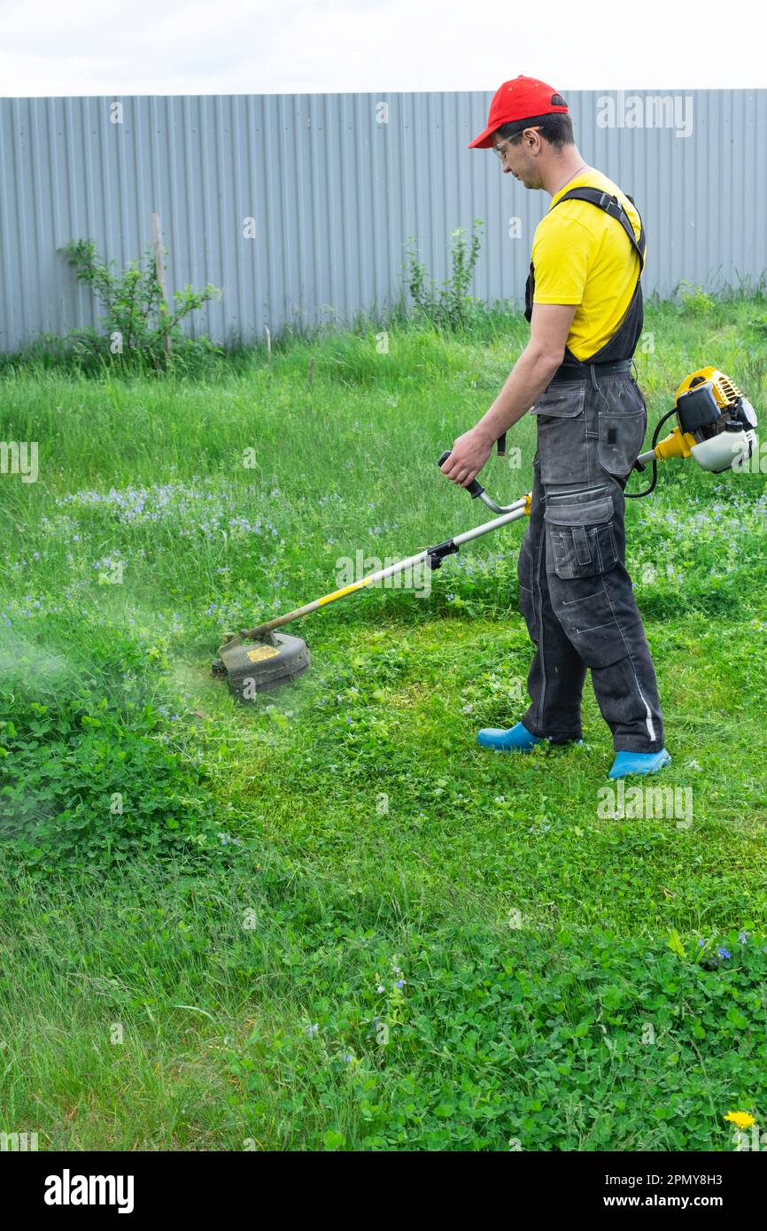 A male gardener mows the green grass of the lawn in the backyard with a ...