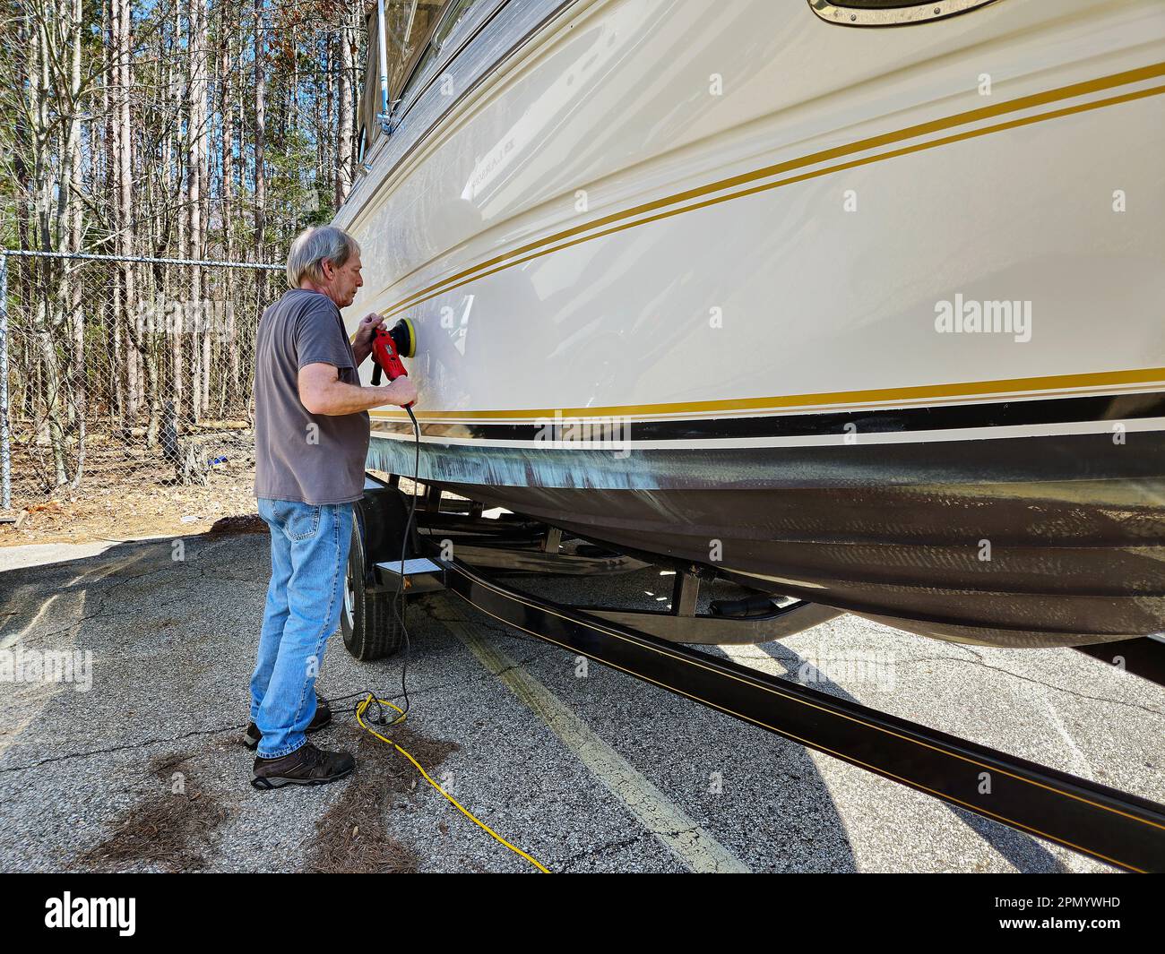 Caucasian man using a portable hand buffing tool on a power boat hull ...