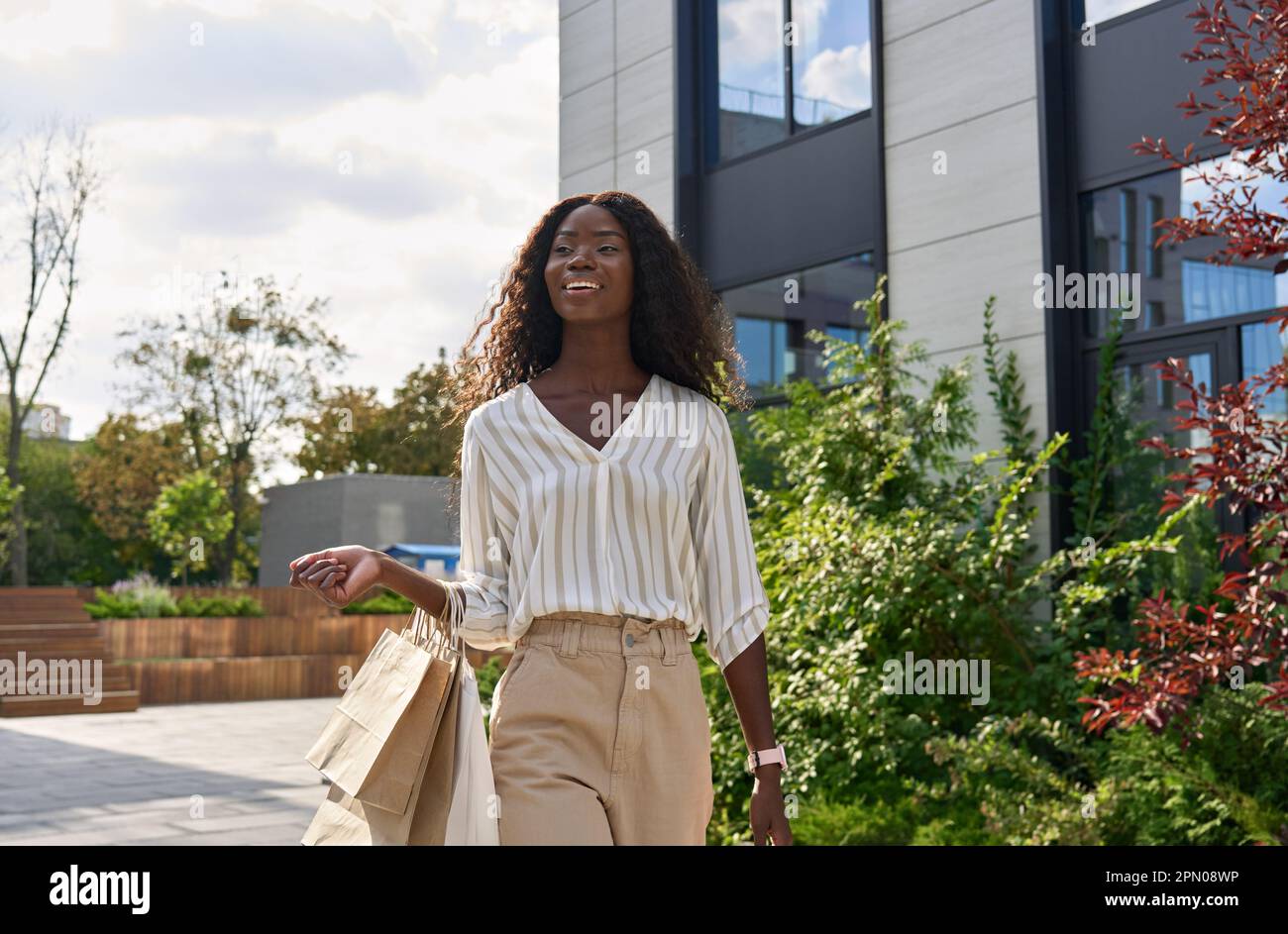 Happy black woman shopper walking on city street holding shopping bags ...