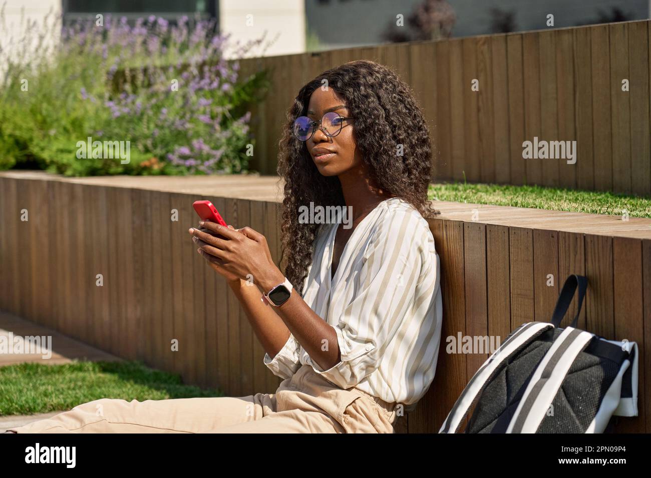 Young African black woman student using mobile phone thinking outdoors ...