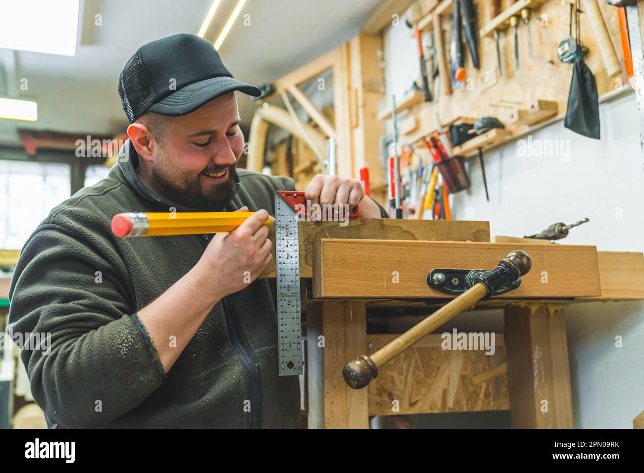Happy male carpenter marking on wood with big pencil. Variety of tools ...