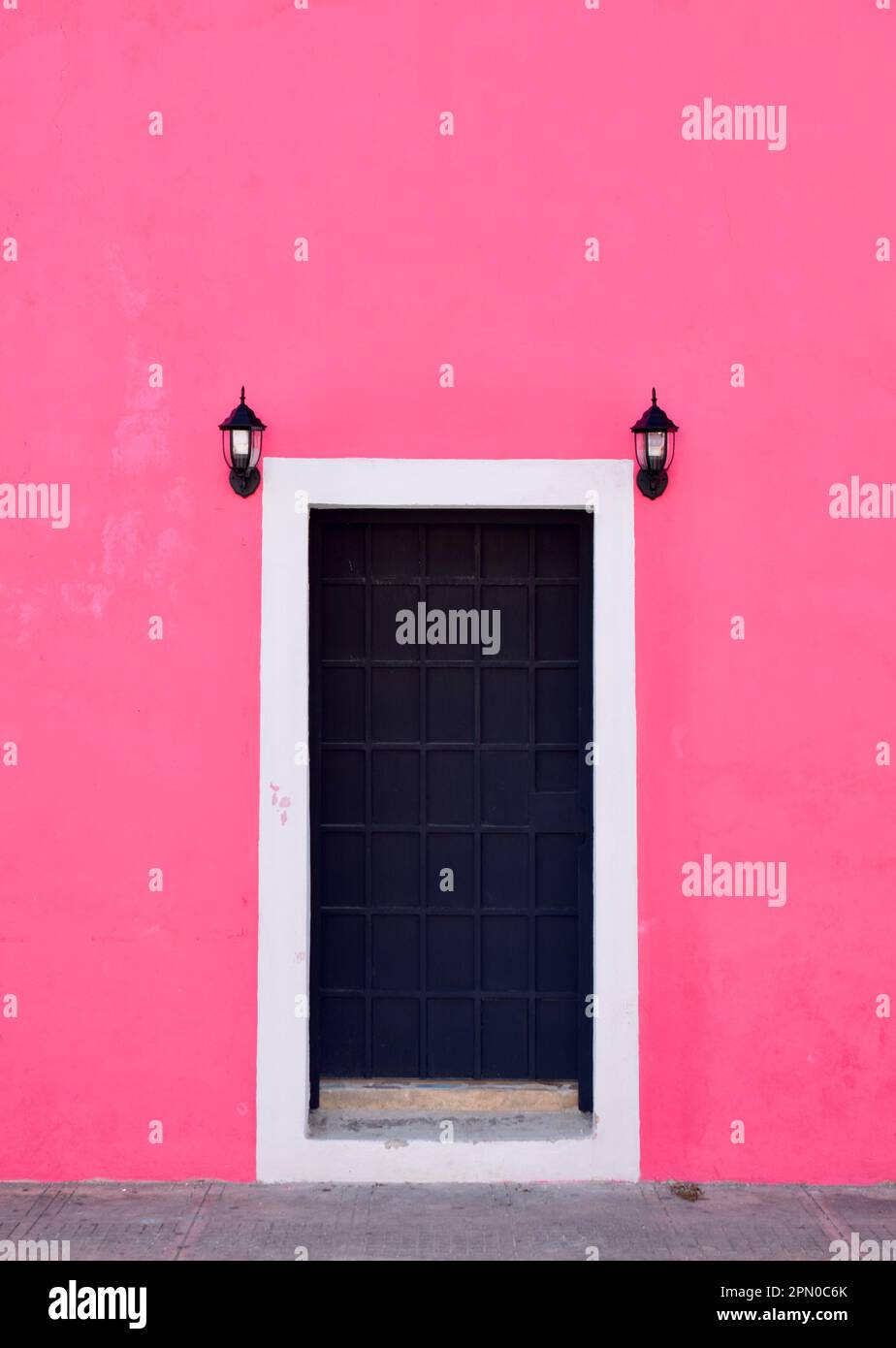 A bright pink building facade and a wooden door with two sconces in a ...
