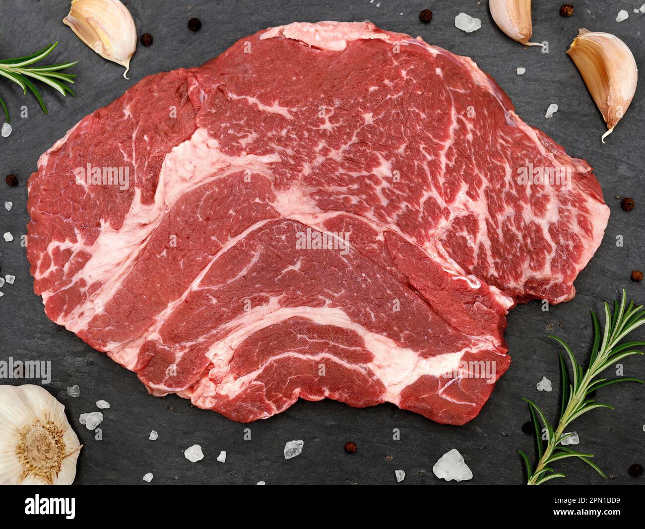 Top view of a raw chuck eye beef steak with herbs, spices and garlic on ...