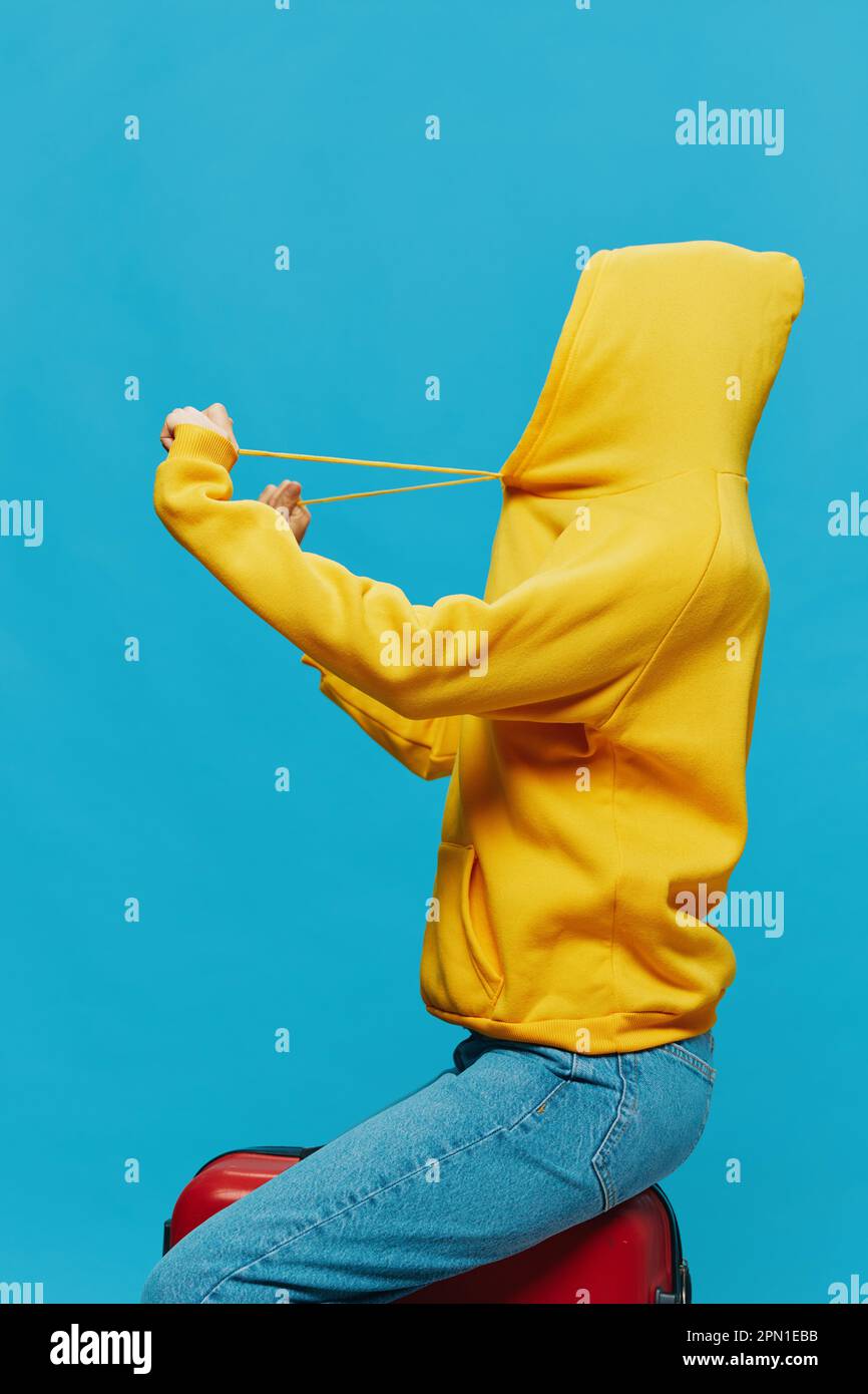Smile woman sitting on a suitcase in a yellow hoodie, blue jeans and ...
