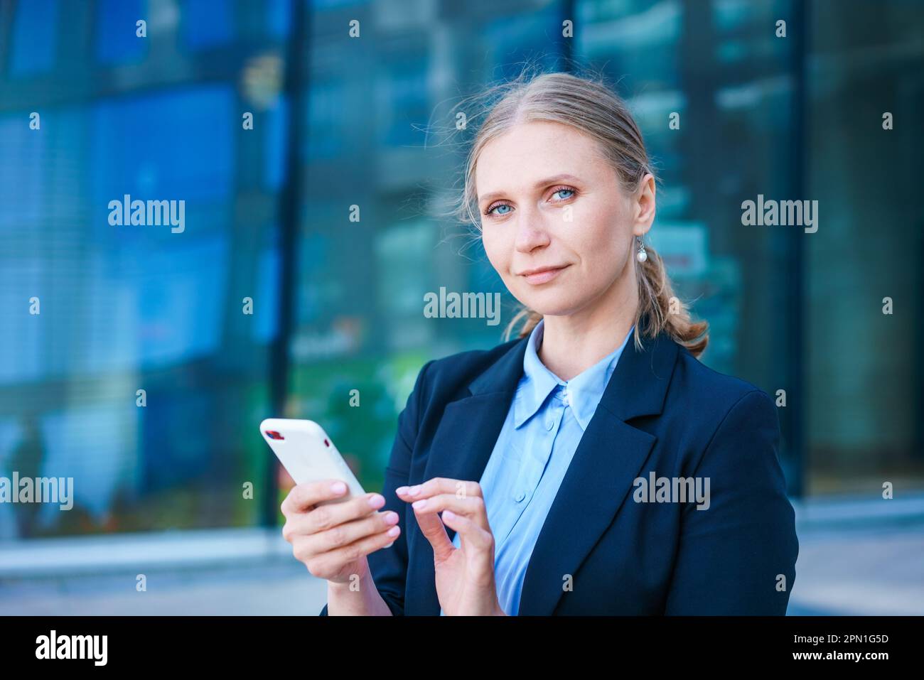 Successful female banker using smart phone outdoors while standing near ...