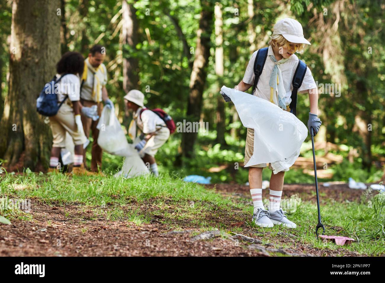 Full length portrait of cute boy as scout helping clean forest during ...