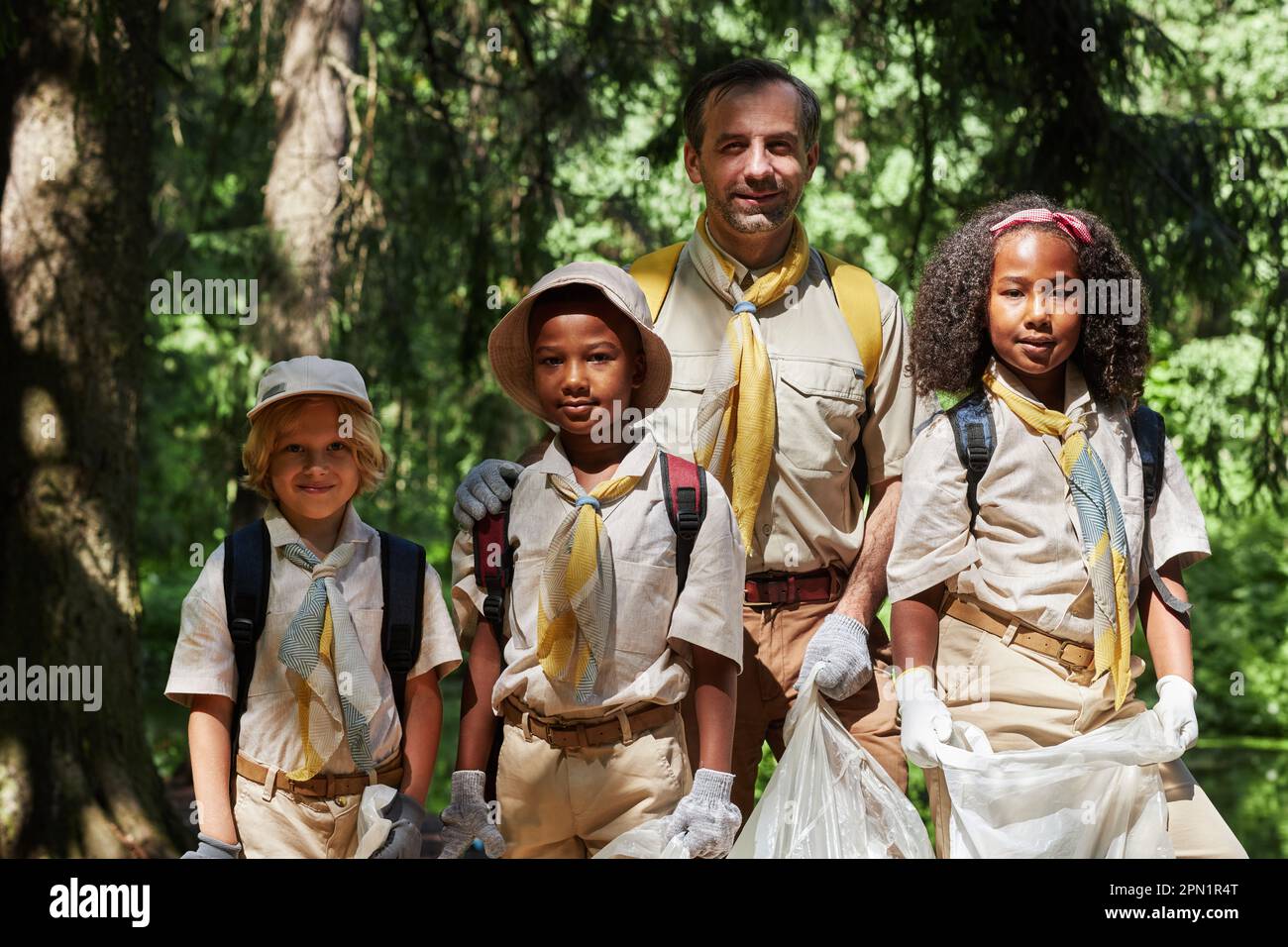 Group of scouts with adult leader looking at camera in forest during ...