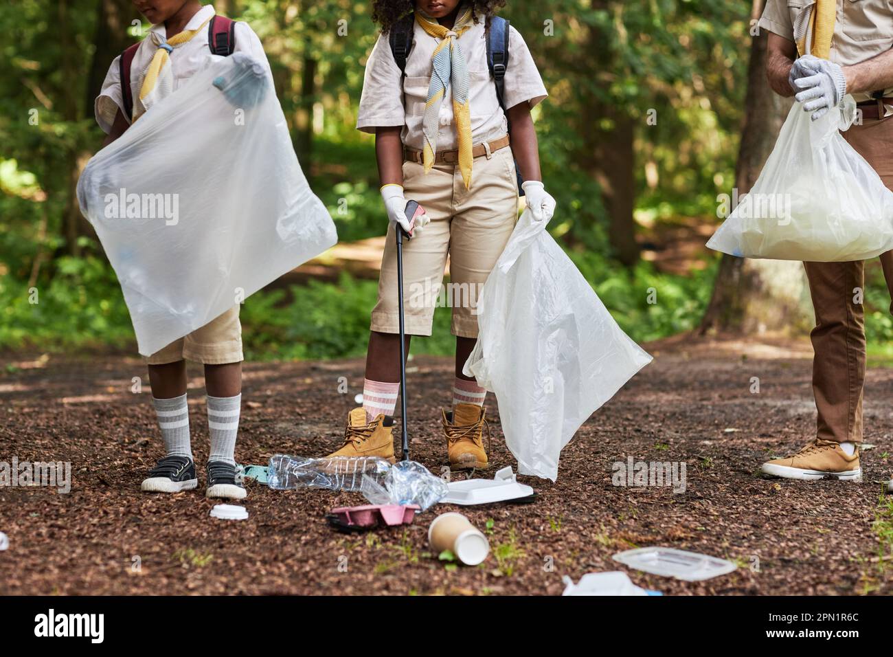 Low section of group of scouts picking up trash in forest during eco ...