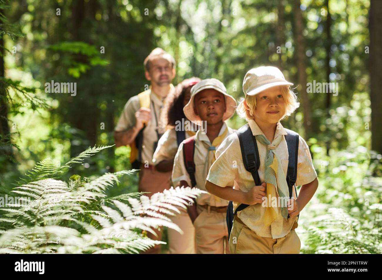 Waist up portrait of cute boy with group of scouts hiking in forest lit ...