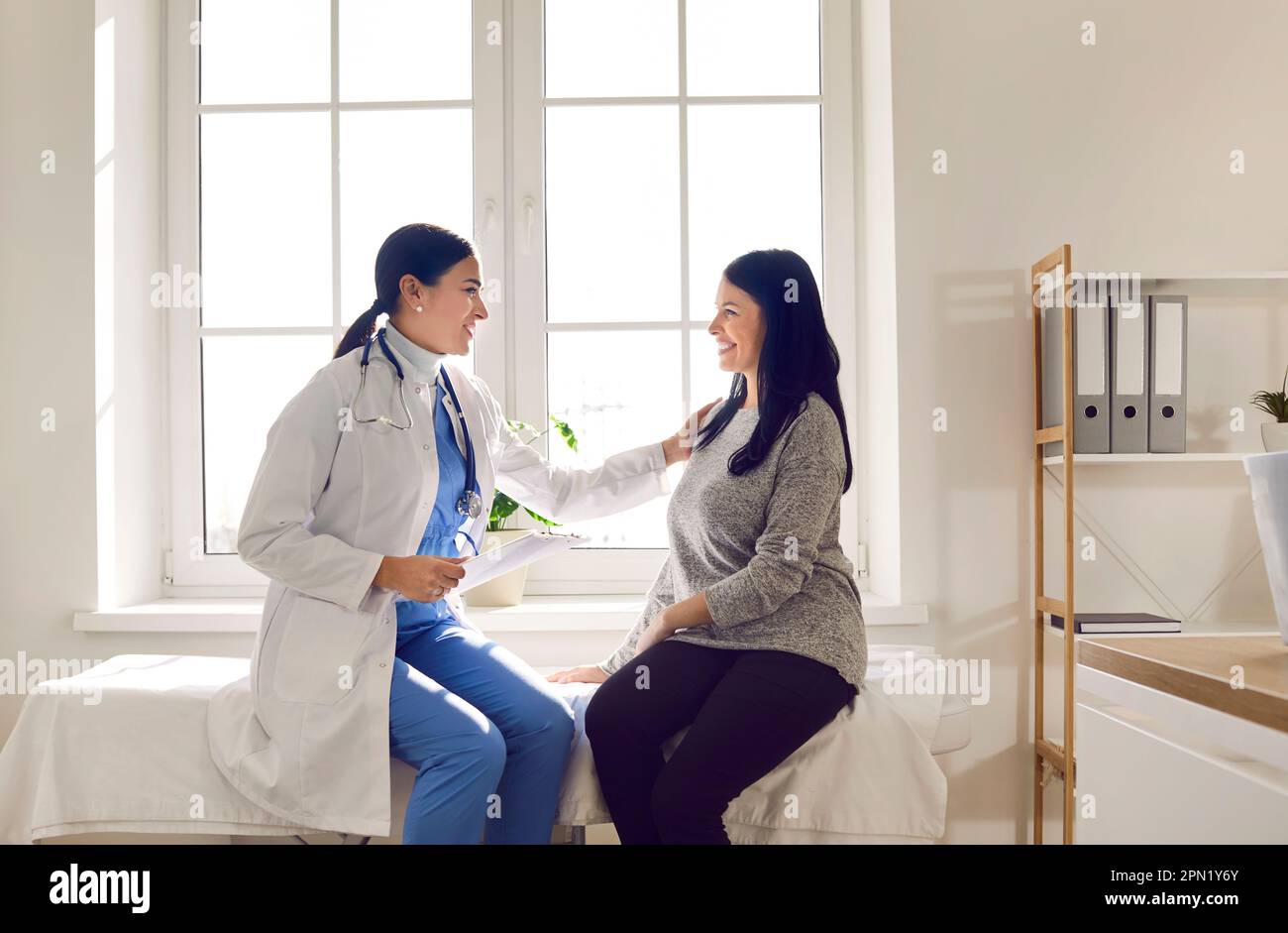 Doctor having conversation with young woman patient, supporting and ...