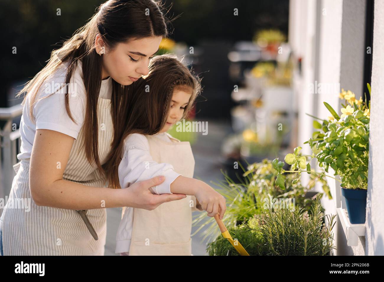 Young mom help her little daughter gardening on balcony. Adorable girl ...
