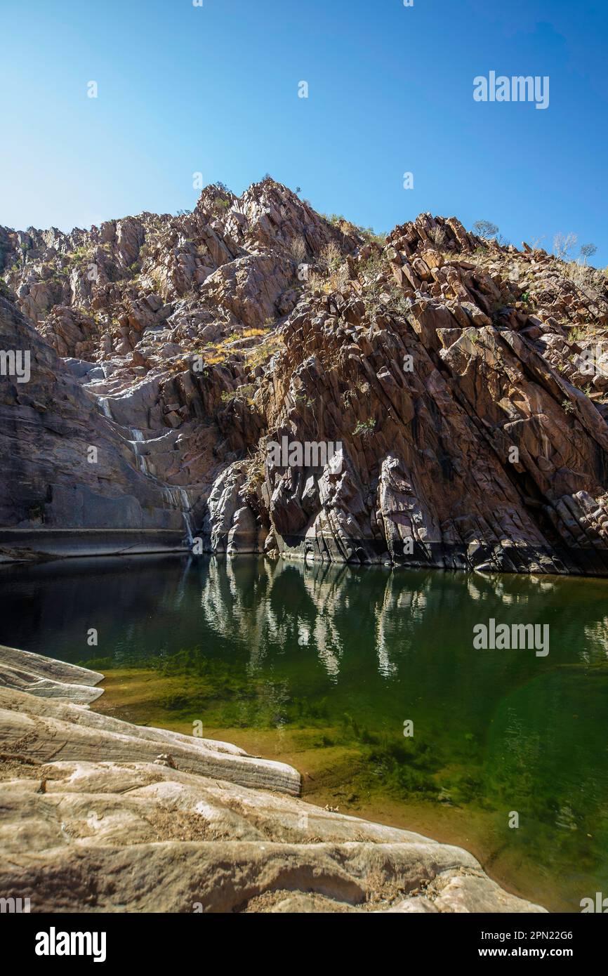 Reflections in the pool beneath a dry waterfall surrounded by rocks ...