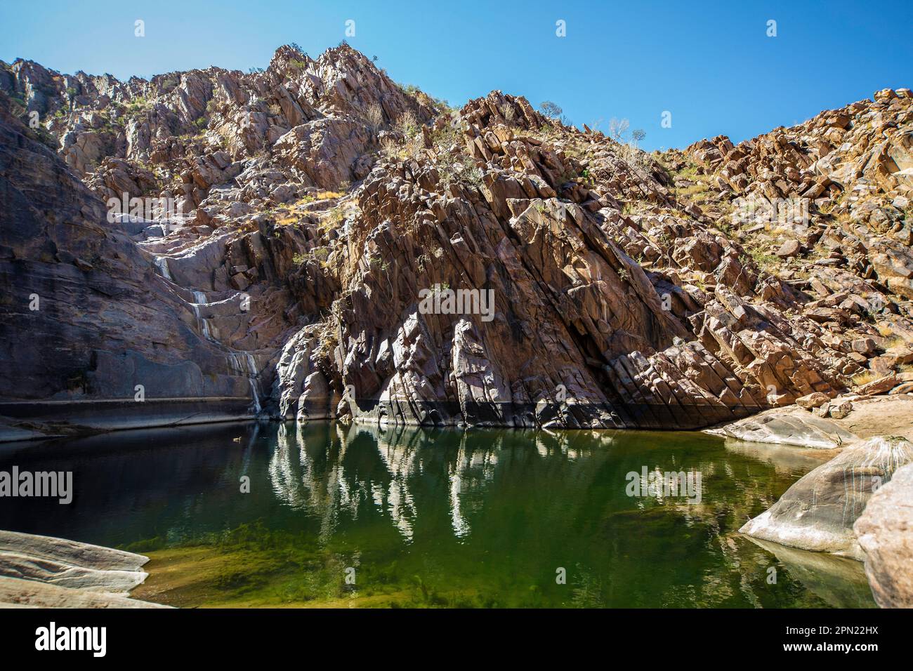 Reflections in the pool beneath a dry waterfall surrounded by rocks ...