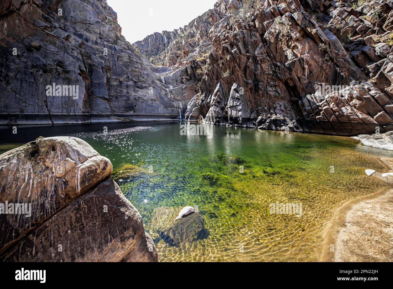 Reflections in the pool beneath a dry waterfall surrounded by rocks ...