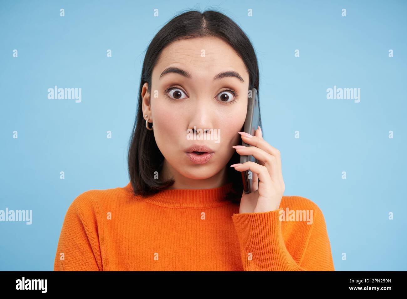 Technology concept. Asian girl answers phone call and looks surprised ...