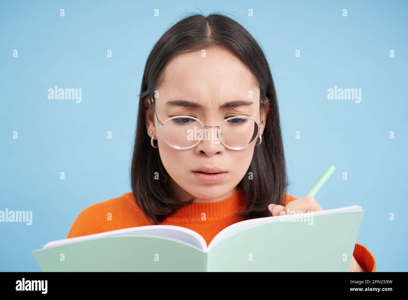 Woman in glasses looking in her notebook with serious face, making ...