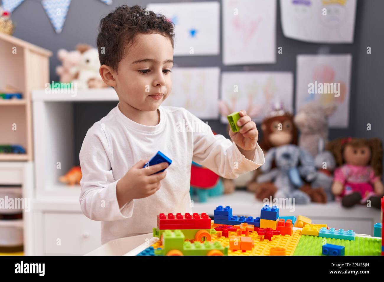 Adorable hispanic boy playing with construction blocks standing at ...
