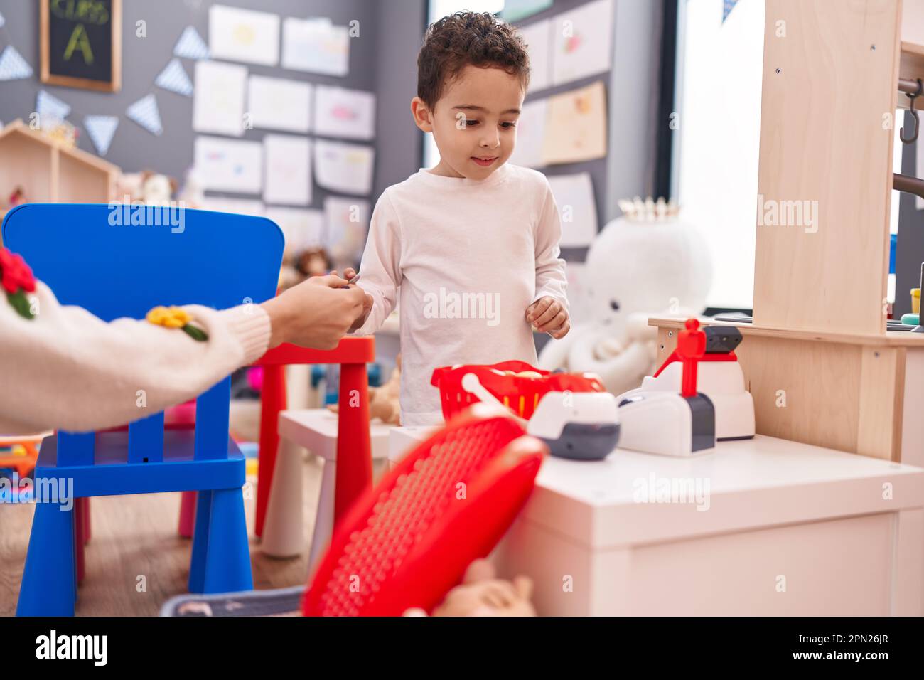 Adorable hispanic boy playing supermarket game standing at kindergarten ...
