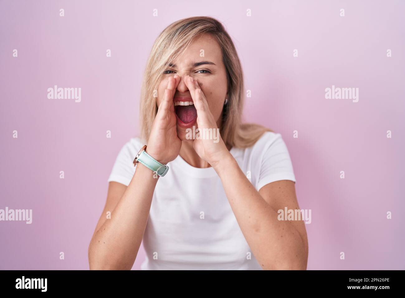 Young blonde woman standing over pink background shouting angry out ...
