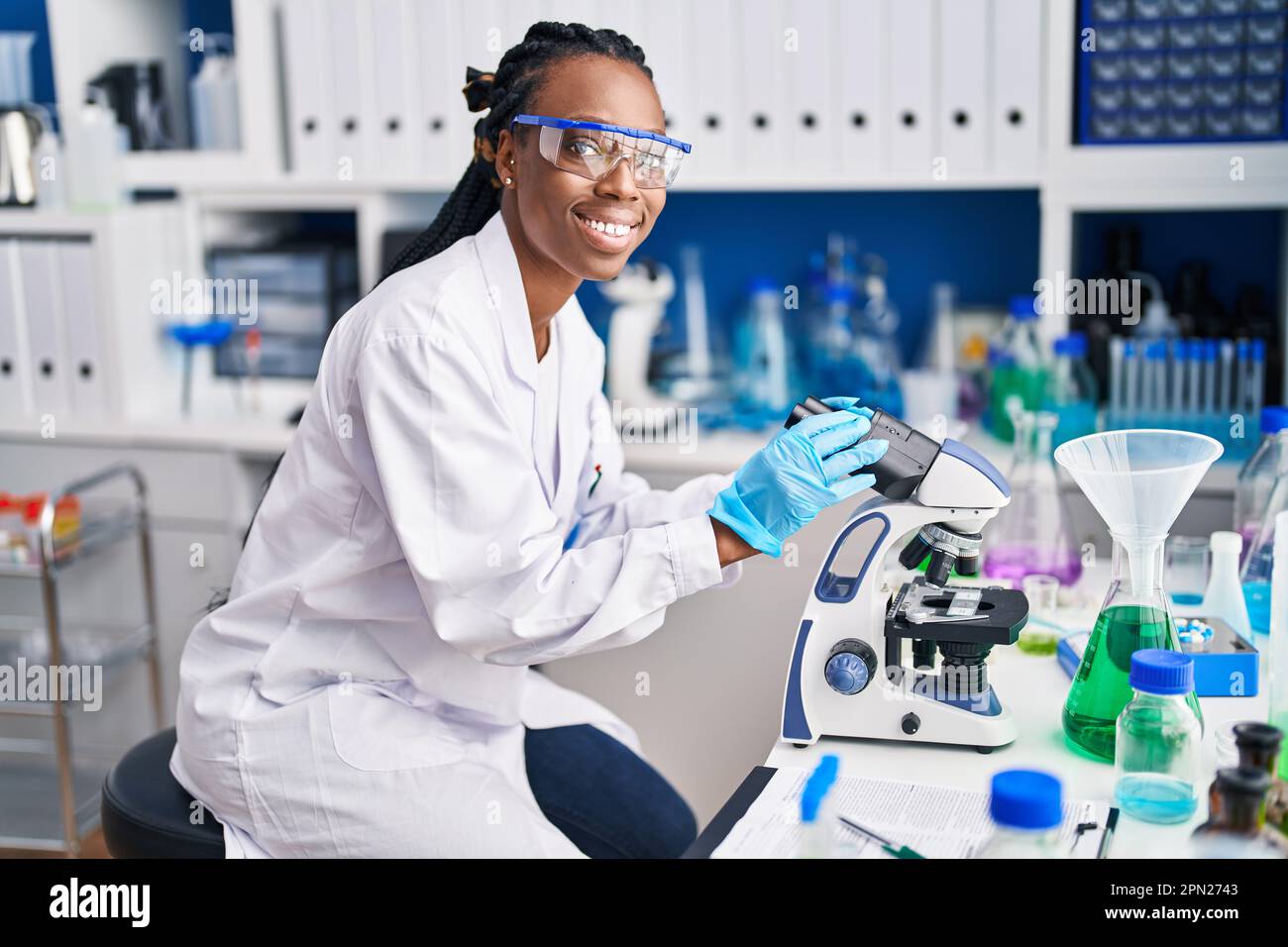 African american woman scientist smiling confident using microscope at laboratory Stock Photo ...