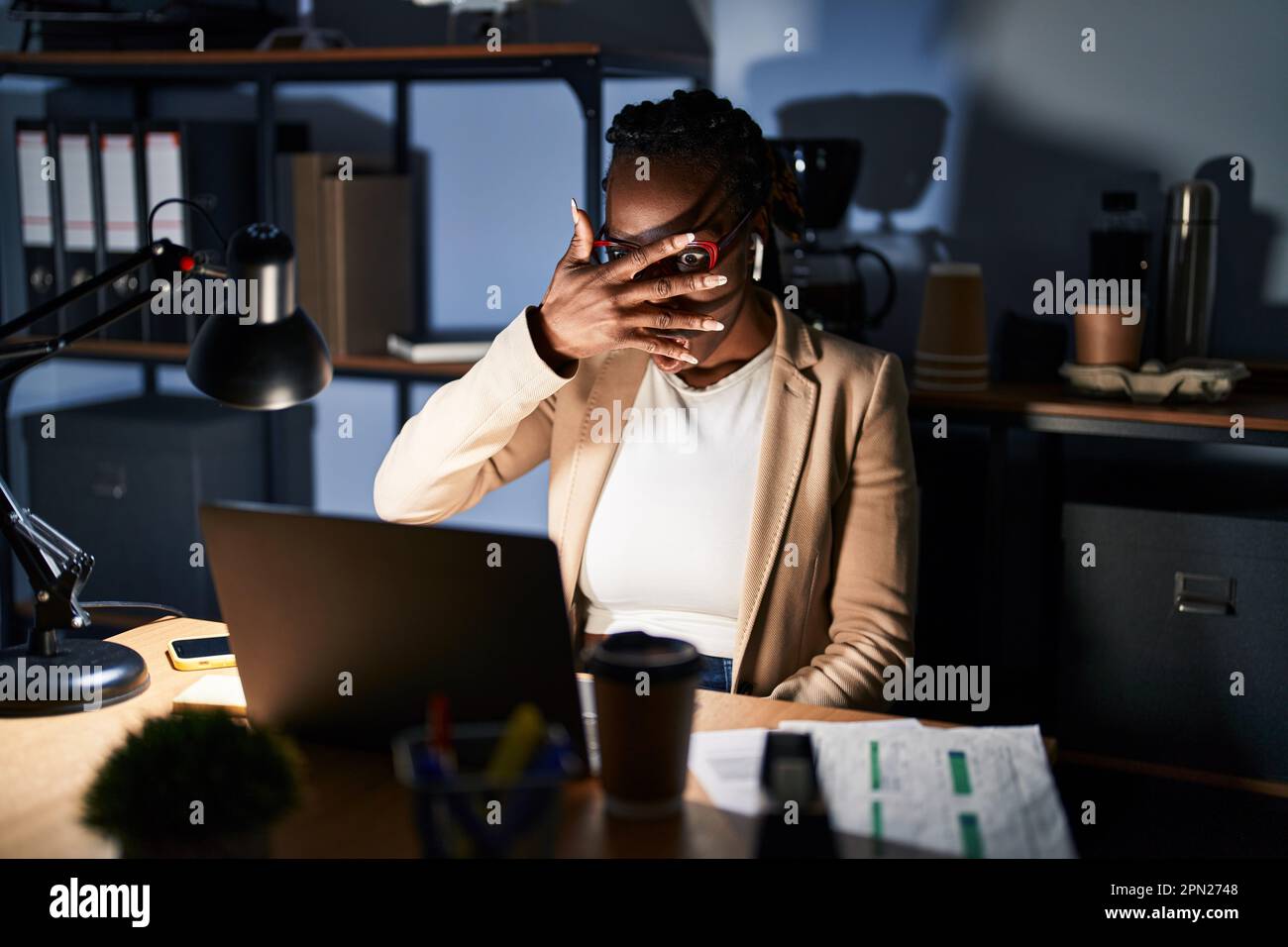 Beautiful black woman working at the office at night peeking in shock ...