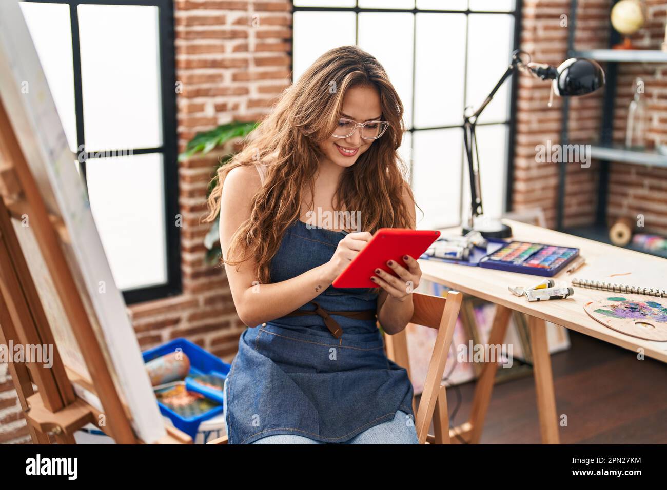 Young beautiful hispanic woman artist using touchpad sitting on chair ...