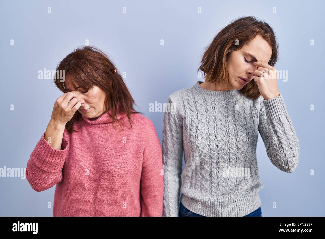 Mother and daughter standing over blue background tired rubbing nose ...