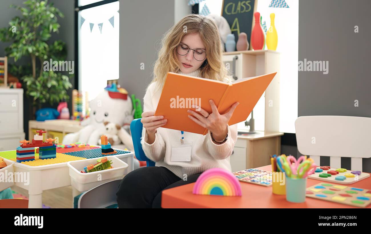 Young blonde woman preschool teacher reading book with relaxed ...