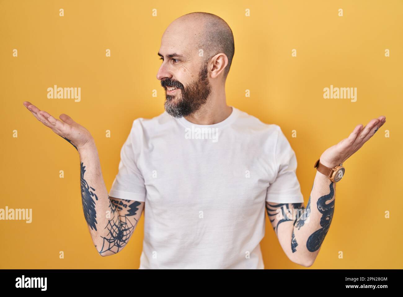 Young hispanic man with tattoos standing over yellow background smiling ...